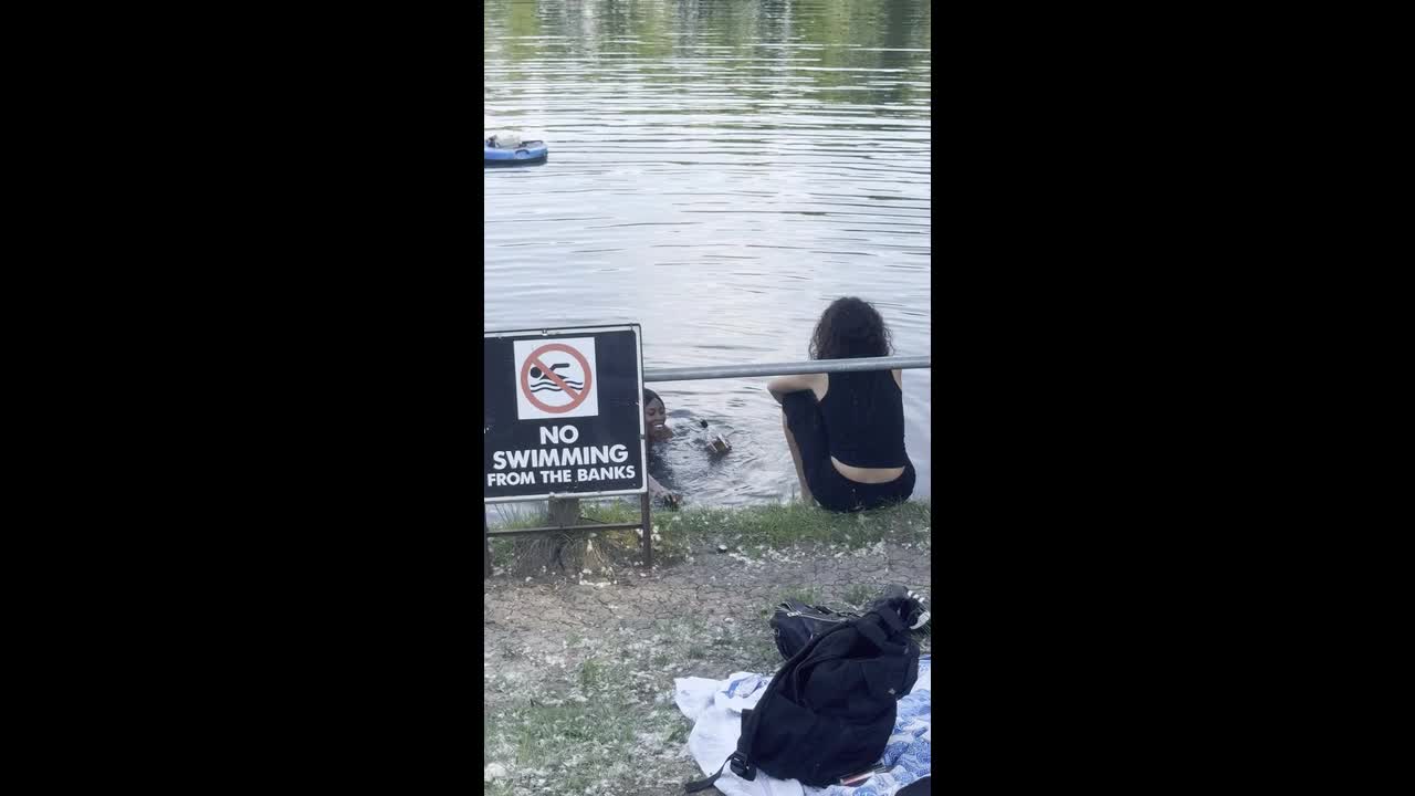 Woman swims with wine bottle in hand, ignoring 'no swimming' signs at ...