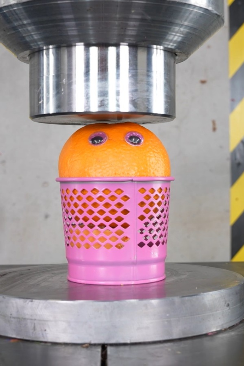 Hydraulische Presse gegen Orange im rosa Korb