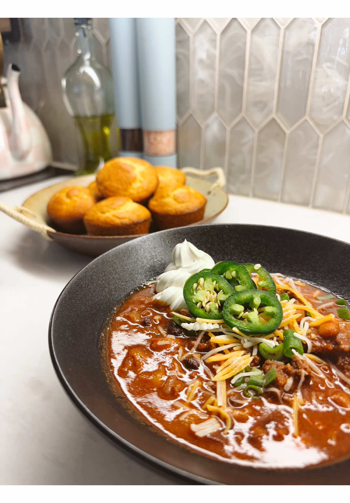 A hearty homemade chili bowl with corn muffins, sour cream, and sliced ...