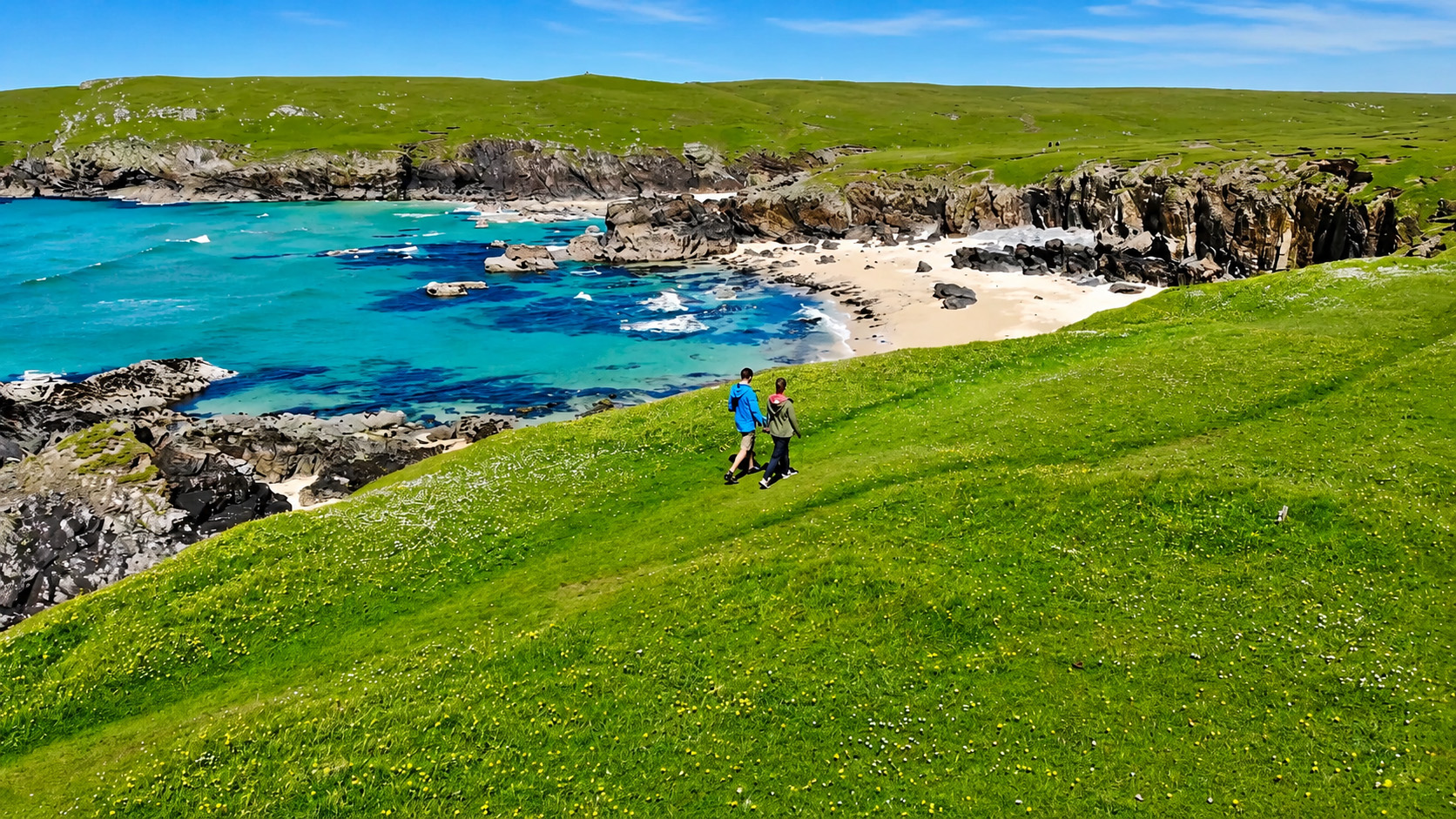 A hidden beach on the Isle of Lewis beneath green cliffs and blue water