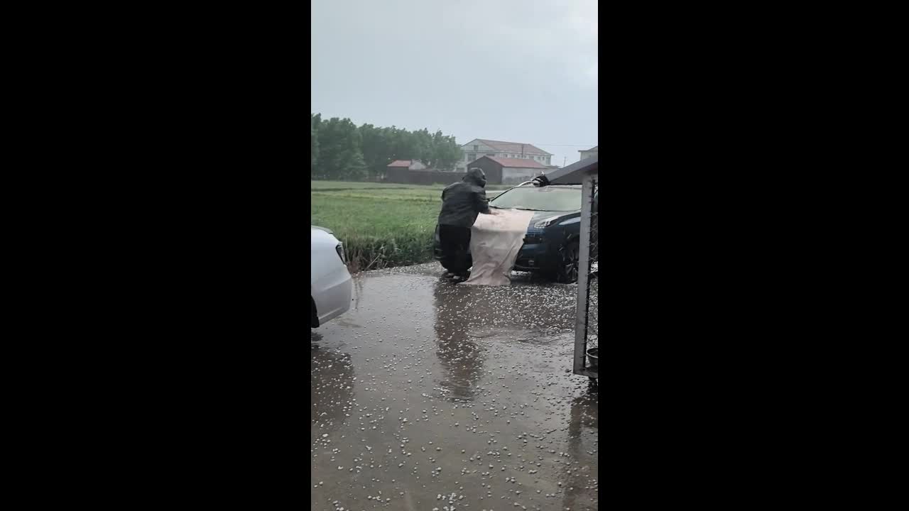 Man struggles to cover car during hailstorm in Jiangsu, China