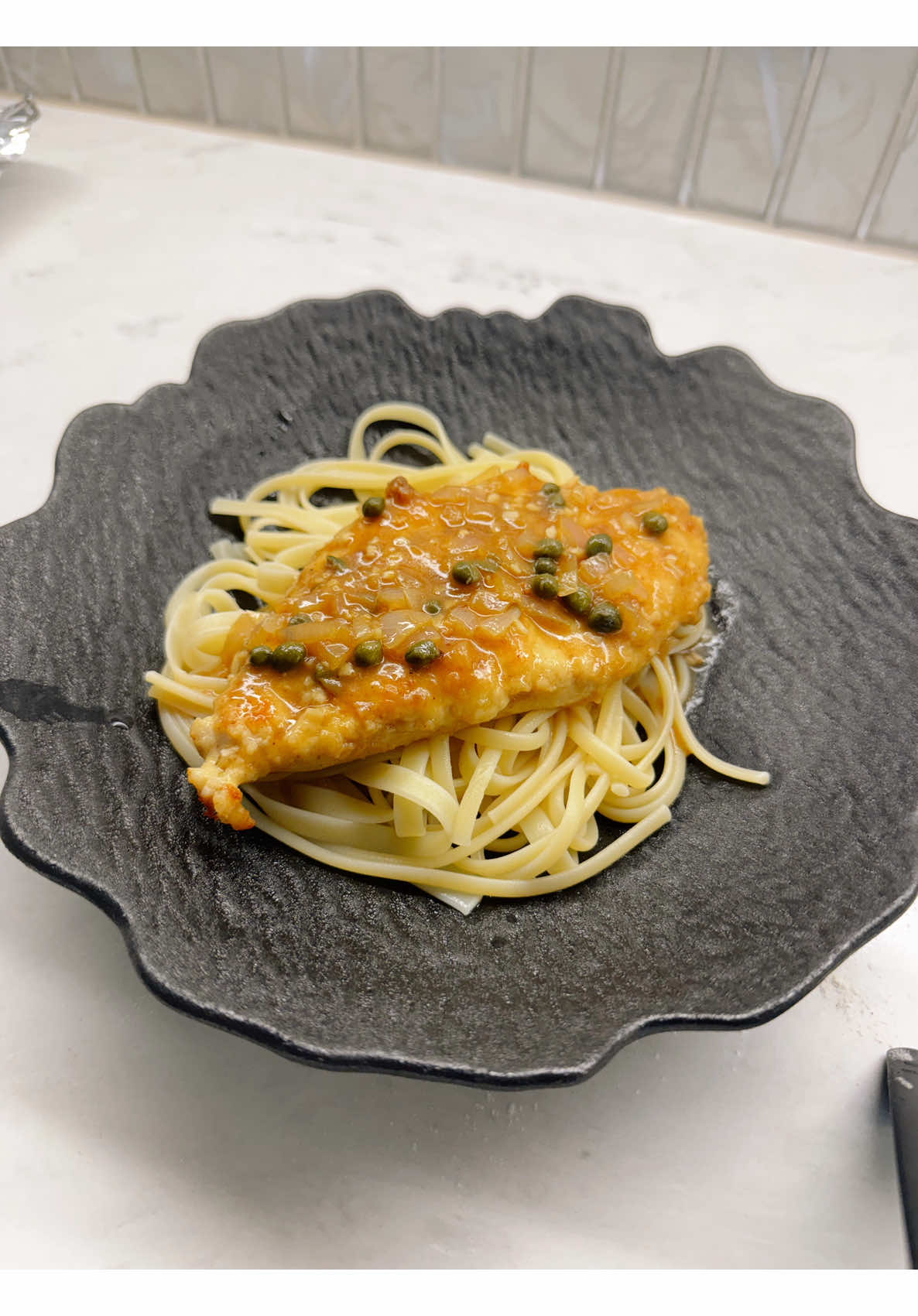 A plate of chicken piccata with linguine in a bright caper and onion ...