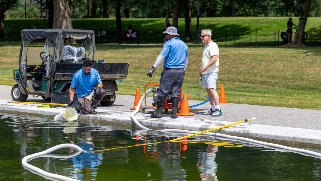 Workers pour hydrogen peroxide into green reflecting pool