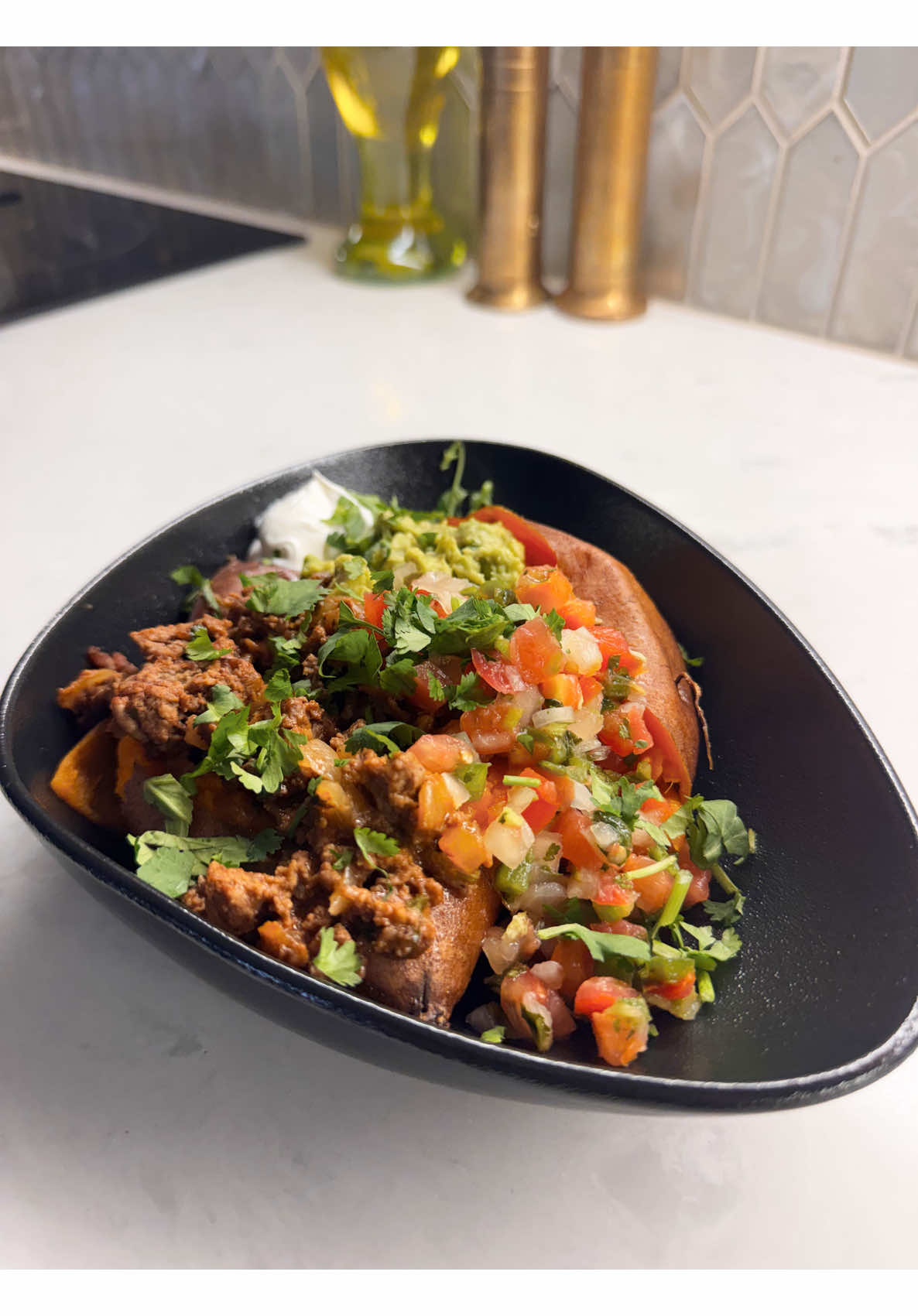 A healthy loaded sweet potato with seasoned ground meat, guacamole, and ...