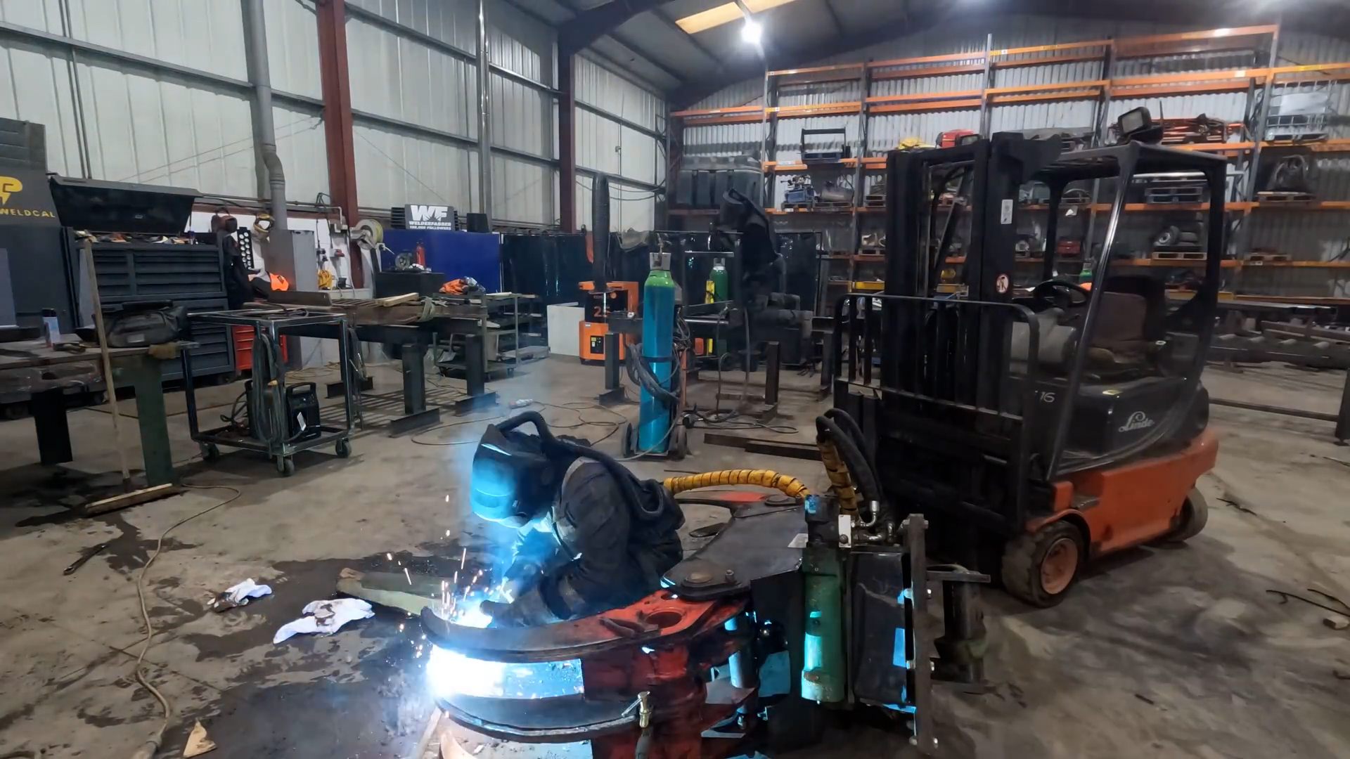 Welder repairing heavy machinery component in industrial fabrication shop