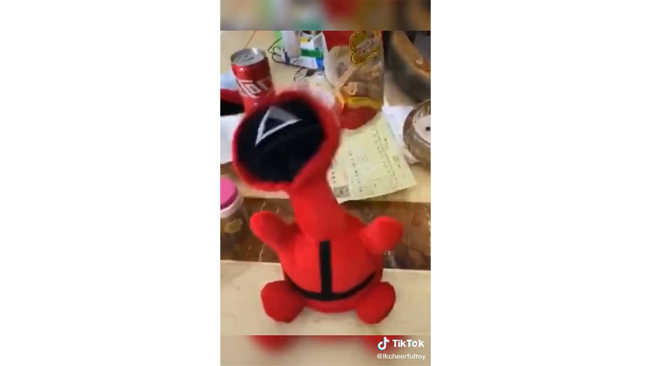 Playing with a red Squid Game guard plush toy with triangle mask