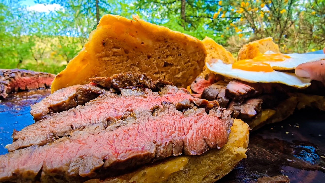 Watch how this steak sandwich sizzles over fire in the forest