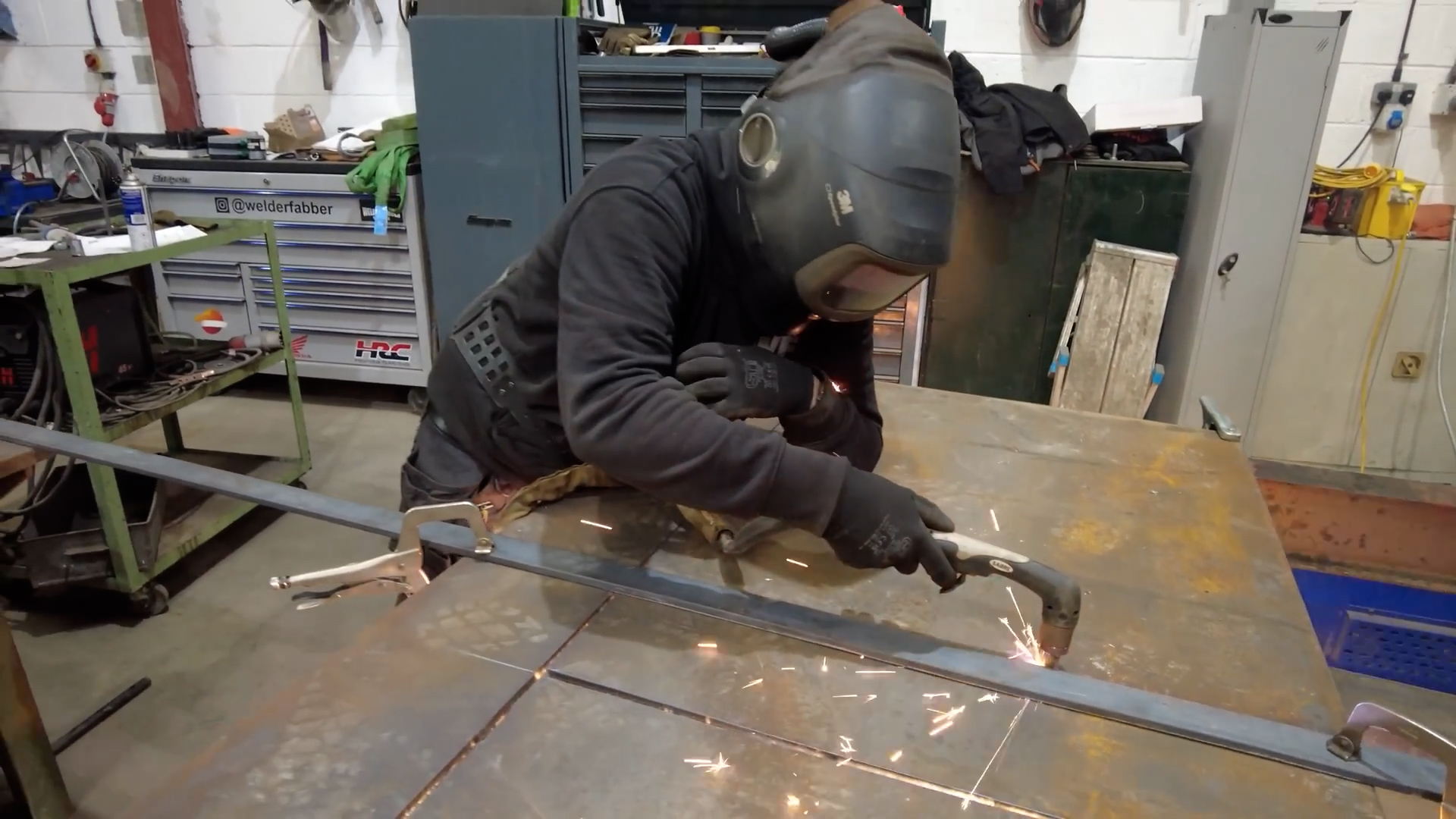 Metal fabricator using plasma cutter to shape steel components in workshop