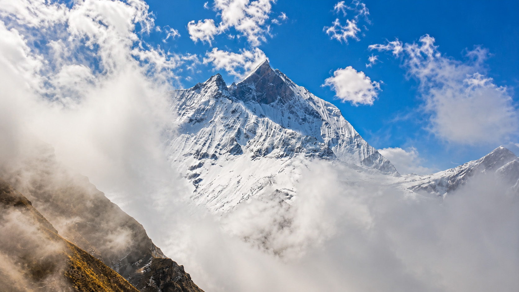 Una montagna innevata che emerge tra nebbia e luce del sole