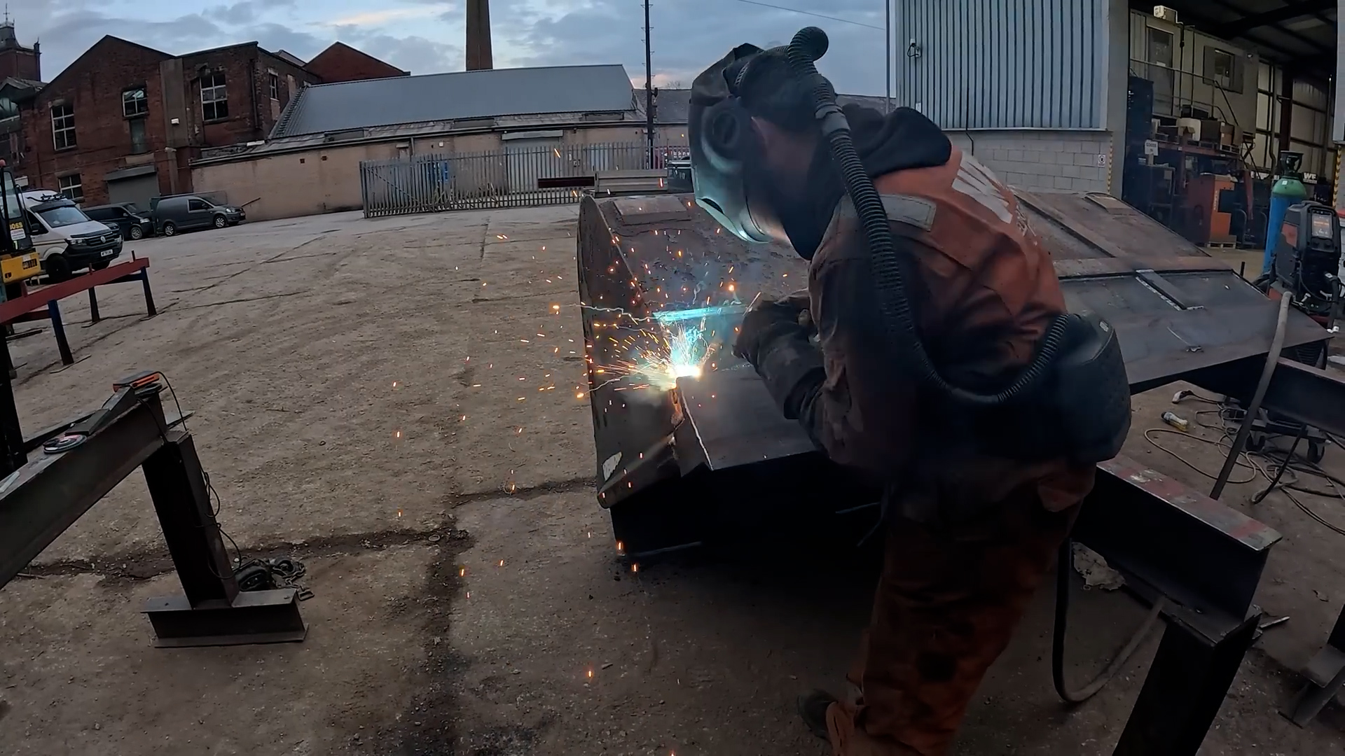 Welder fabricating heavy-duty steel truck wash ramp in industrial yard