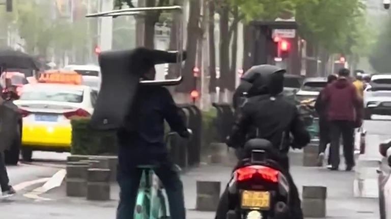 Cyclist uses chair as makeshift umbrella during rainstorm