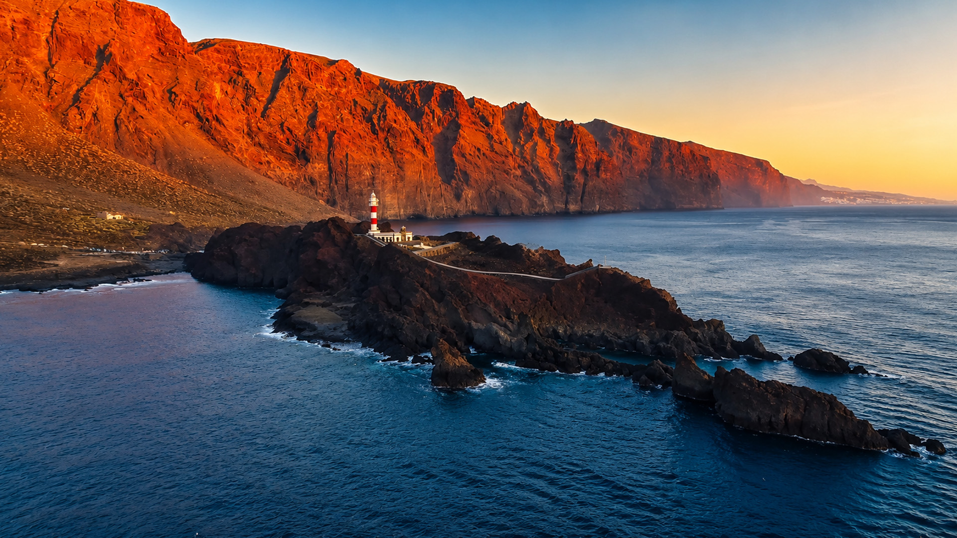 A lighthouse standing below giant sea cliffs