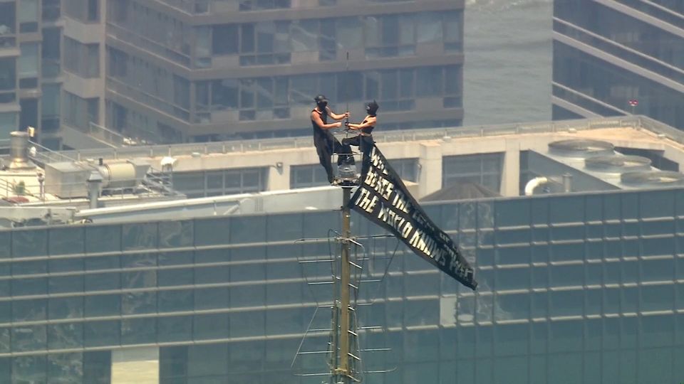 Two people scale to the top of the Empire State Building holding banner