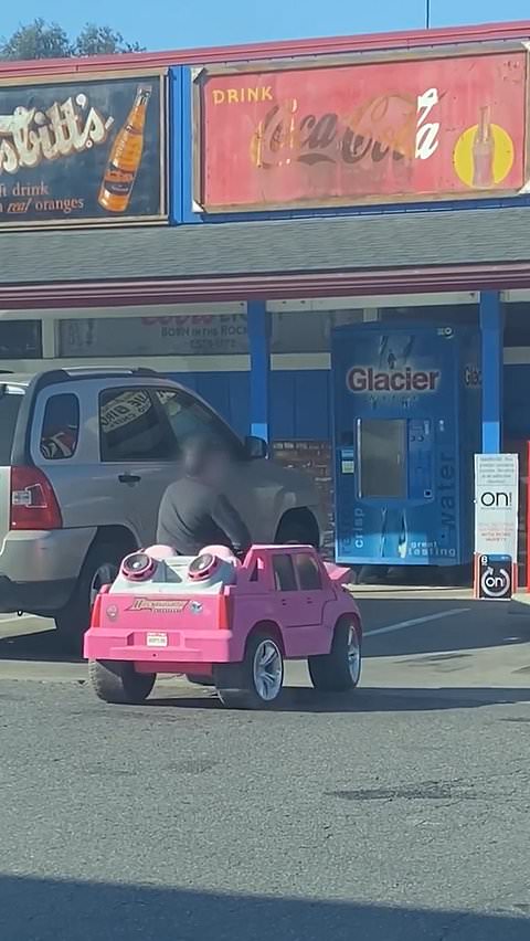 Child drives pink toy car outside convenience store